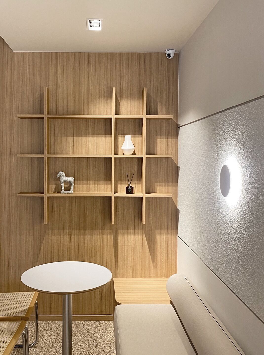 Quarto moderno com parede de madeira, uma mesa redonda, um banco e uma prateleira com objetos decorativos.
