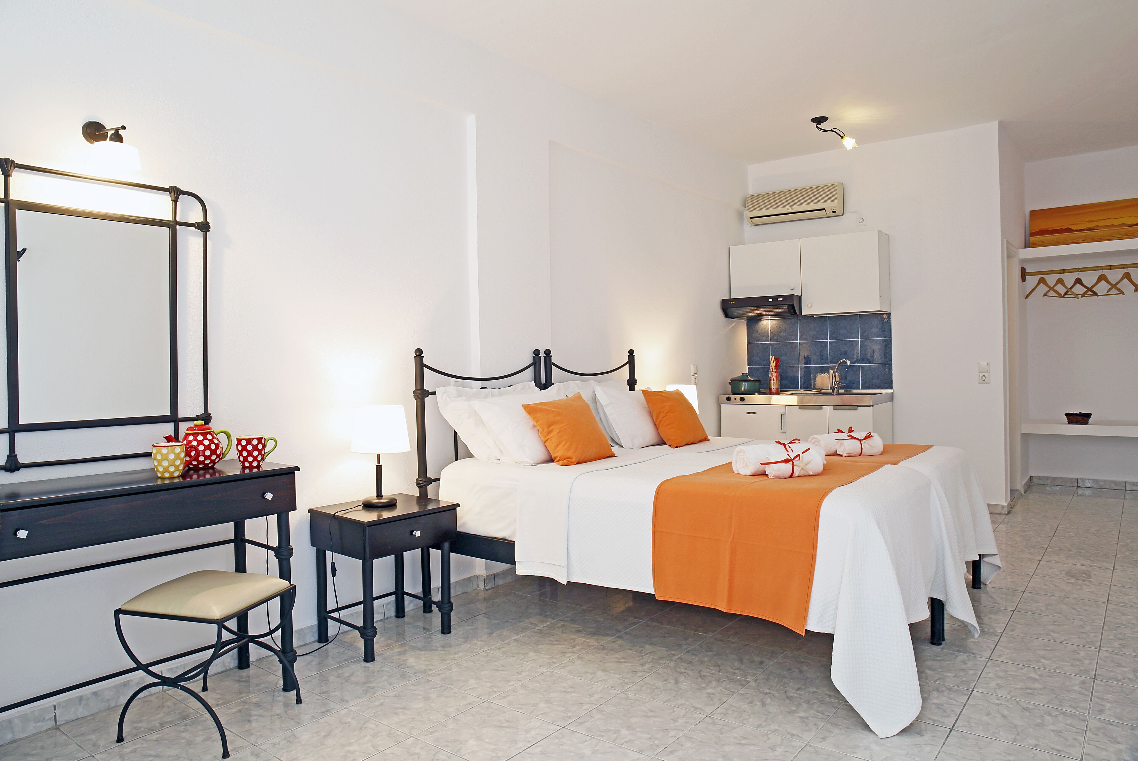 Quarto com cama, escrivaninha, cadeira, mesa de cabeceira e área de banheiro com pia e espelho.