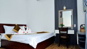 Quarto de hotel com cama de madeira, uma escrivaninha, uma cadeira e um espelho.