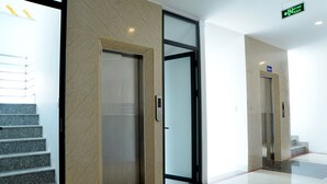 Elevador moderno com parede de mármore, porta de vidro e placa indicando a saída.