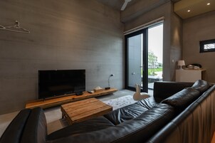 Uma sala de estar moderna com uma grande televisão de tela plana, sofá de couro, mesa de centro de madeira e uma porta de vidro deslizante que dá para uma área externa.