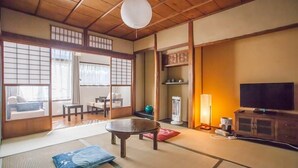 Um quarto japonês tradicional com tatames, uma mesa baixa, uma televisão e uma porta deslizante que dá para outro espaço.