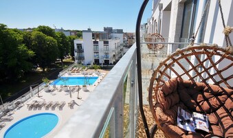 Área de piscina no terraço com espreguiçadeiras e uma piscina pequena, cercada por edifícios e árvores.