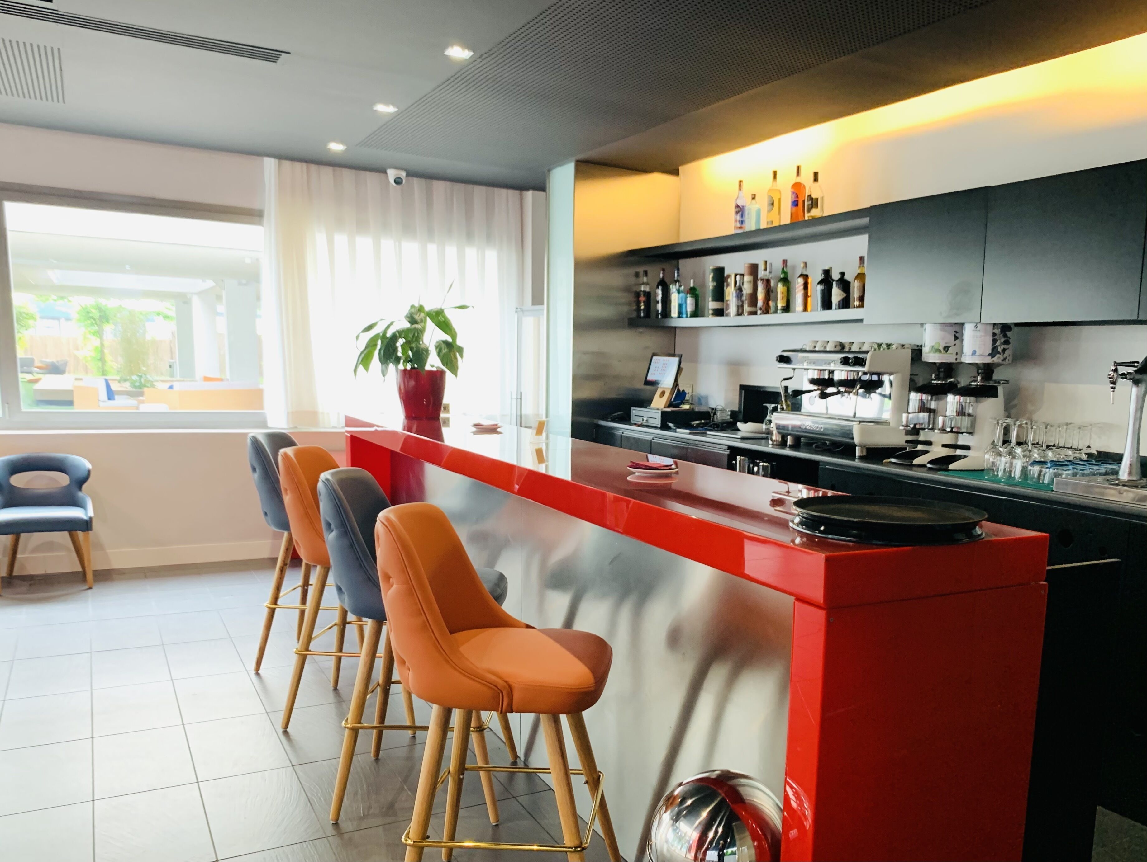 Uma área de bar moderna com balcão vermelho, banquetas e uma máquina de café.