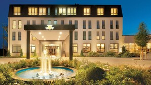Um hotel moderno com uma entrada bem iluminada, uma fonte e um jardim paisagístico.