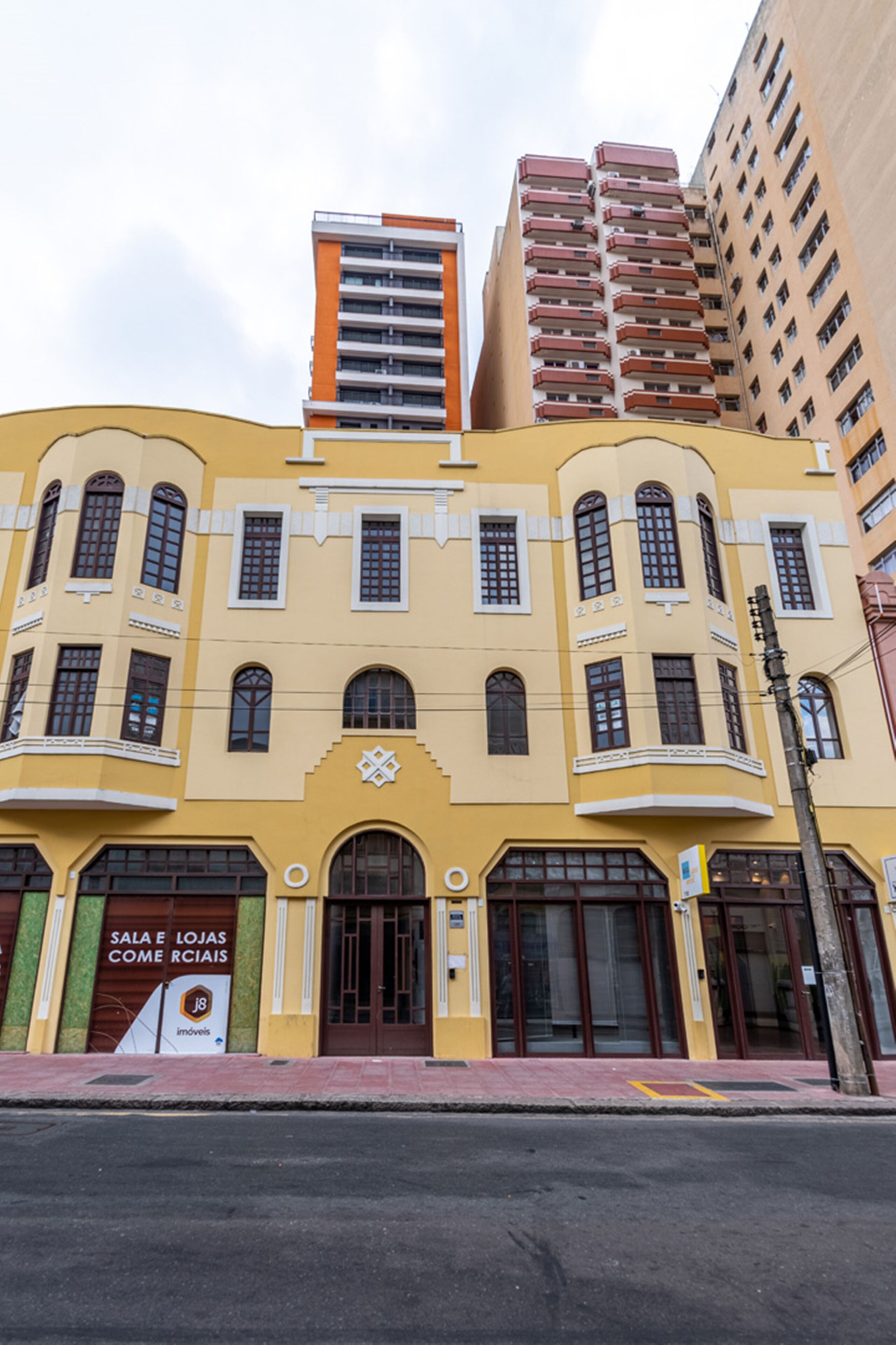 Um edifício amarelo com uma placa que diz "SALA E LOJAS COMERCIAIS" e uma grande janela com um desenho em formato de estrela.