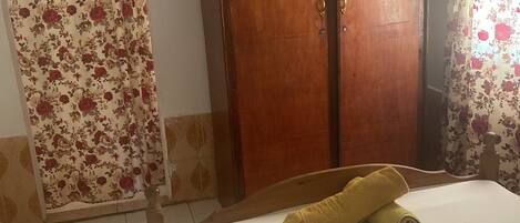 Quarto de hotel com uma cama, um guarda-roupa de madeira e cortinas florais.