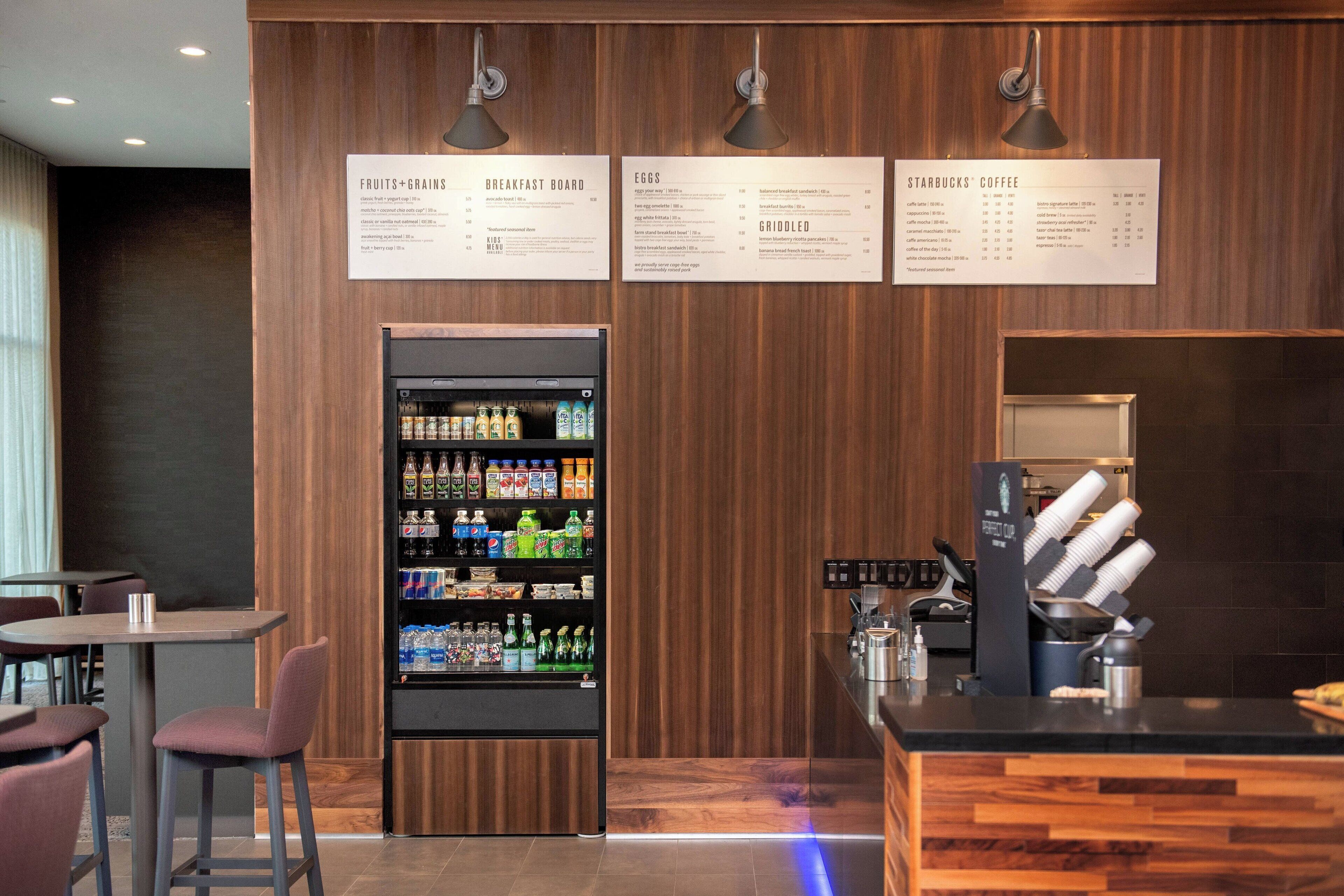Um saguão de hotel moderno com bar de café da manhã, máquina de vendas automática e espaço para café.