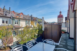 Um pátio com mesa e cadeiras, um galpão de madeira e uma torre do relógio ao fundo.