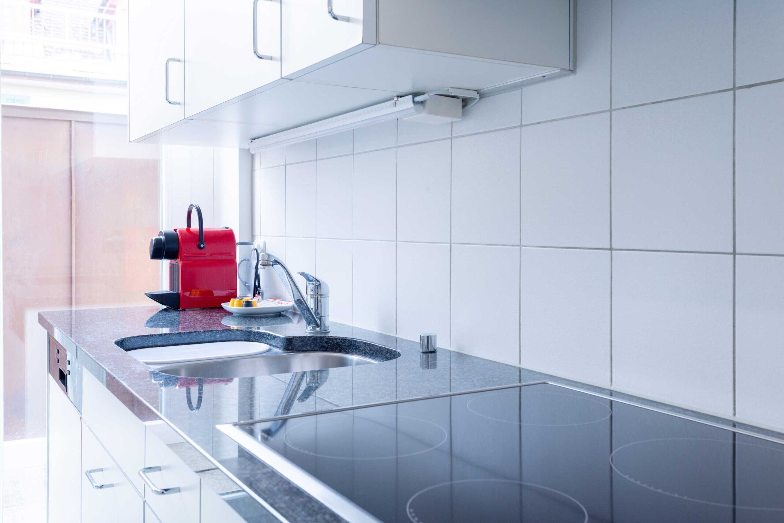 Cozinha moderna com bancada preta, pia de aço inoxidável e armários brancos.