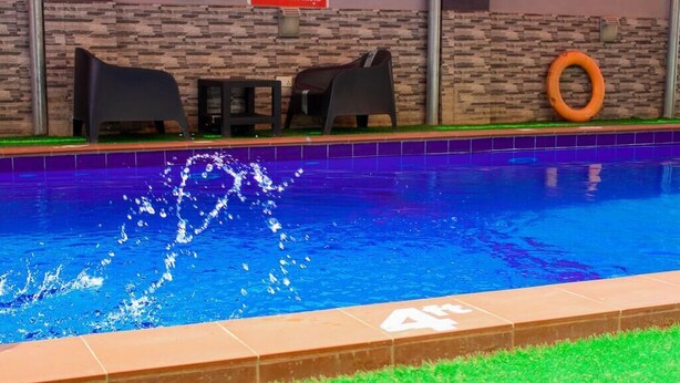 Uma piscina com um elemento aquático, um flutuador de segurança e uma placa com a inscrição "POR SUA CONTA E RISCO".