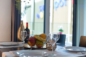 Mesa de jantar posta com pratos, talheres, uma tigela de frutas, copos de vinho e um castiçal decorativo.