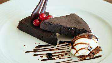 Sobremesa em um prato branco com pedaço de chocolate, frutas vermelhas e uma bola de sorvete com calda de chocolate.