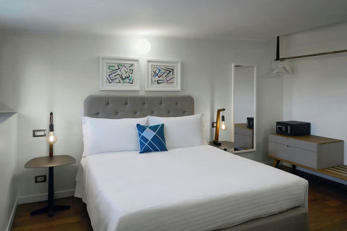 Quarto bem organizado com uma cama grande, uma mesa de cabeceira com abajur, cômoda e duas obras de arte abstratas emolduradas na parede.