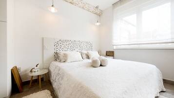 Quarto com cama grande, mesa de cabeceira, mesinha redonda e cabeceira decorativa.