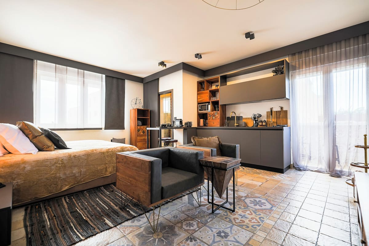 Um apartamento moderno com uma cama grande, um sofá, uma mesa pequena e uma área de cozinha.