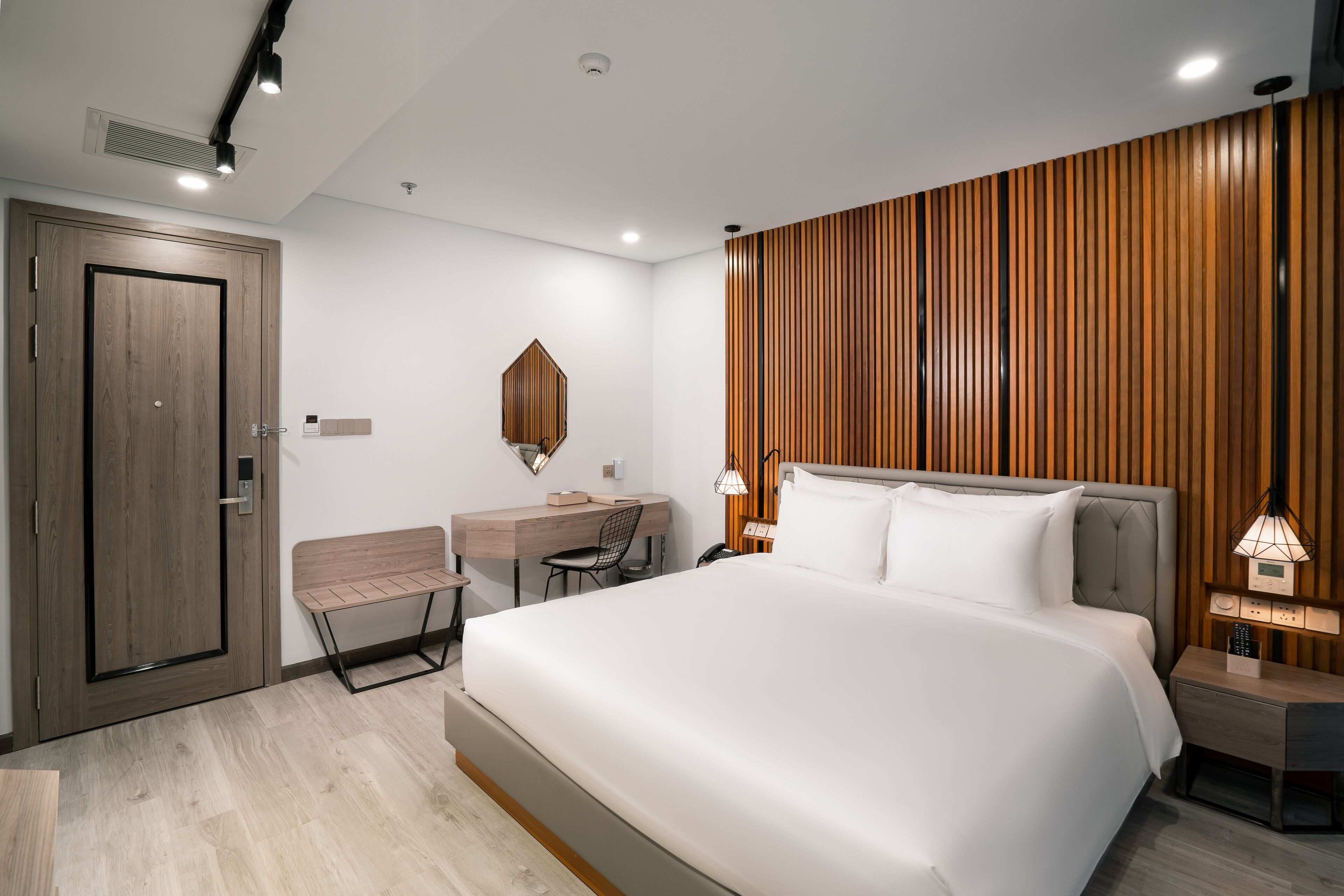 Quarto de hotel moderno com uma cama grande, uma mesa de trabalho com cadeira, painel de parede de madeira e porta de madeira.