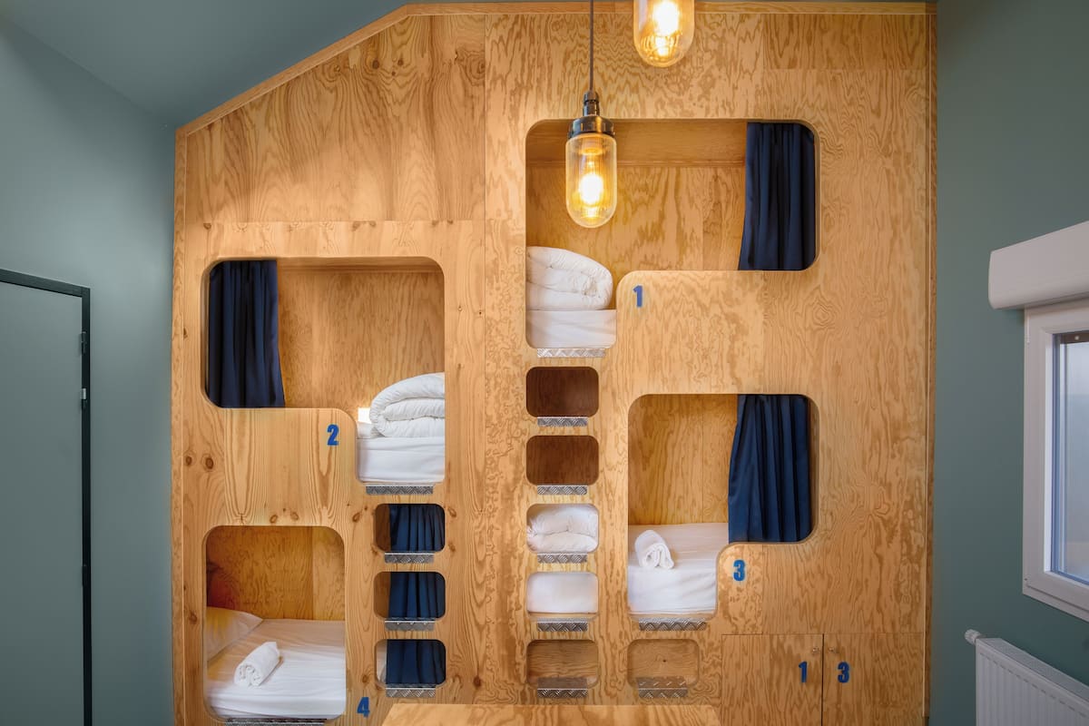 Quarto com beliche de madeira em três níveis, numerados 1, 2 e 3, e luminária pendente.