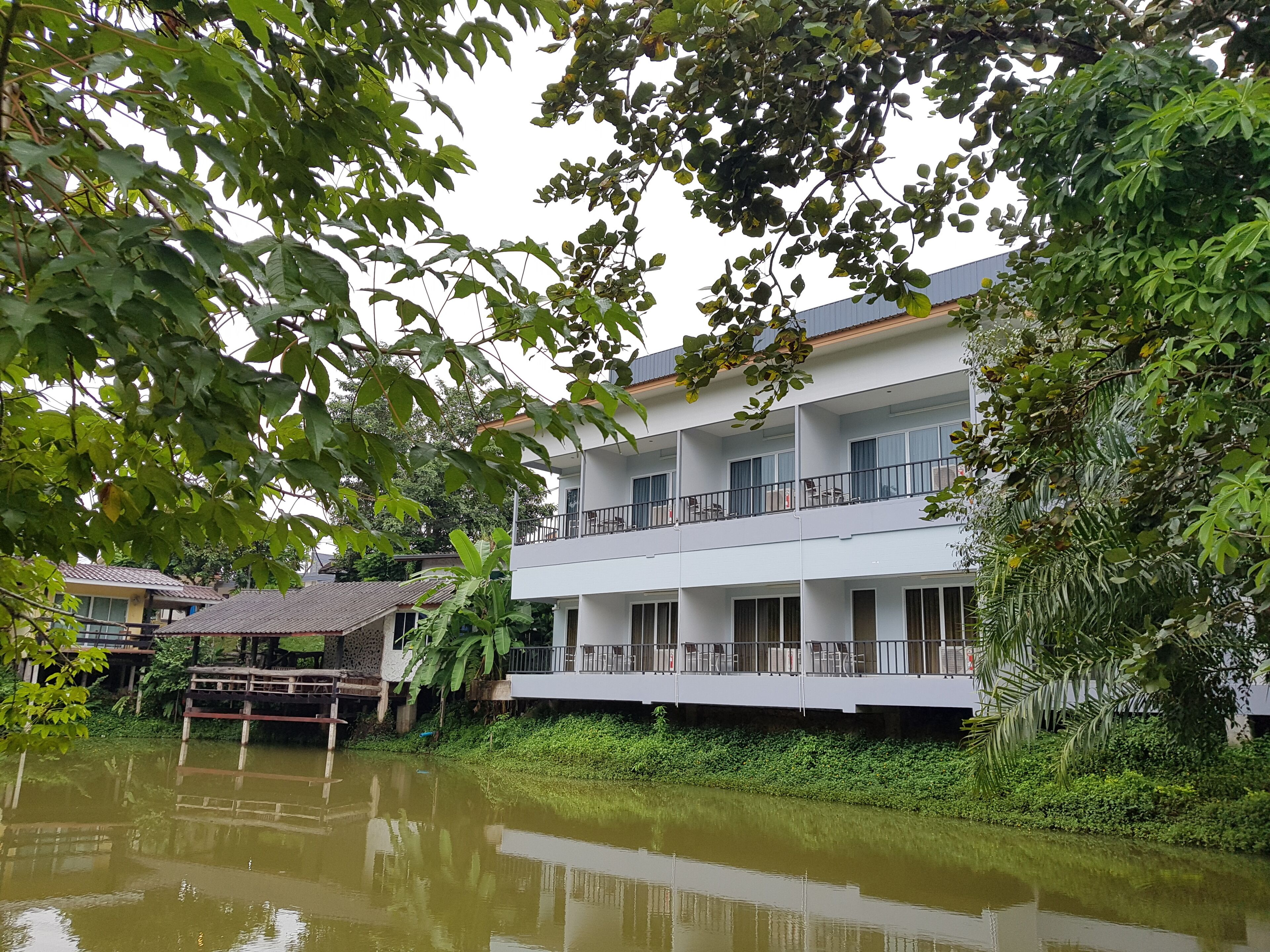 Um hotel com vários andares, varandas, um rio na frente e vegetação exuberante.