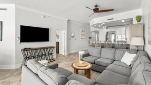Uma sala de estar moderna com um sofá seccional cinza, uma TV de tela plana e um ventilador de teto.
