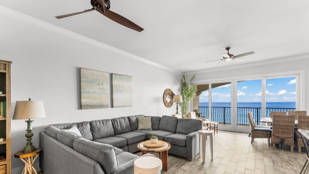 Uma sala de estar ampla com um sofá modular cinza, mesas laterais de madeira e vista para o oceano através de grandes janelas.