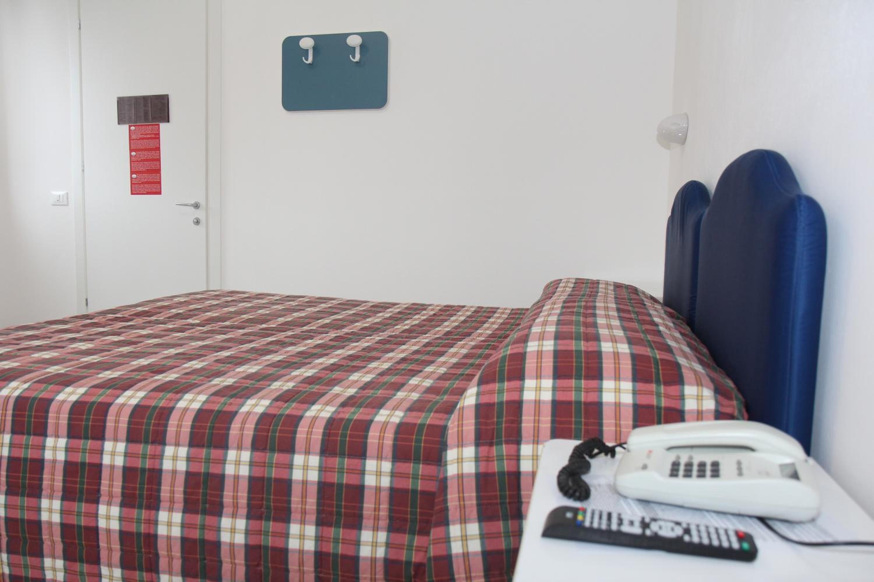 Quarto de hotel com colcha xadrez, telefone e controle remoto na mesa de cabeceira.