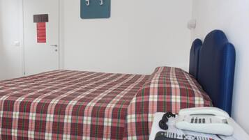 Quarto de hotel com colcha xadrez, telefone e controle remoto na mesa de cabeceira.