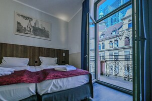Quarto de hotel com uma cama, um quadro na parede e vista para edifícios pela janela.