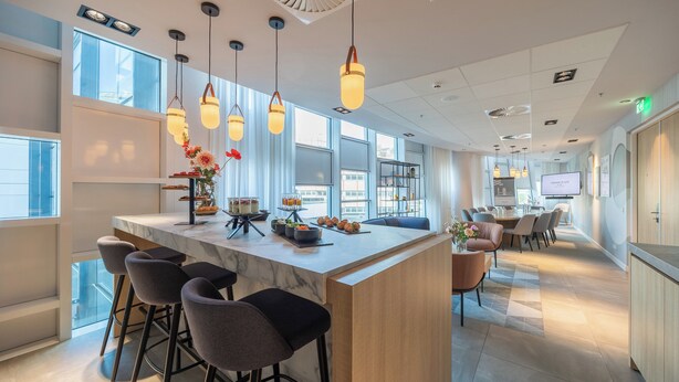 Cozinha moderna com ilha de mármore, banquetas, luminárias pendentes e vista para a cidade.