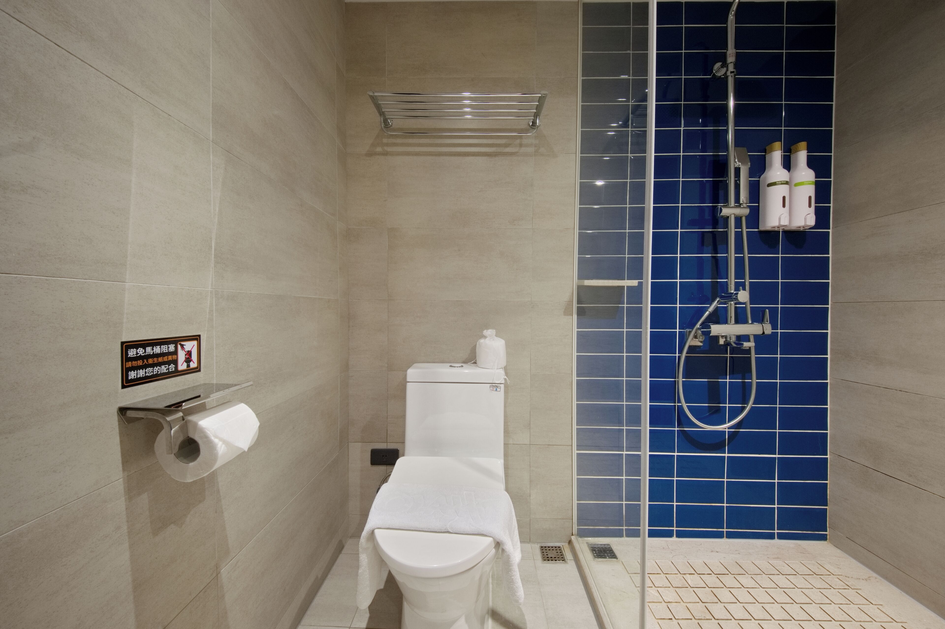 Uma casa de banho moderna com sanita, chuveiro e porta-toalhas.
