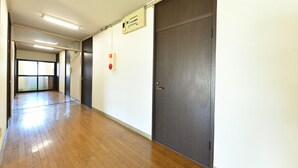 Um corredor com piso de madeira, uma porta fechada e um interruptor na parede.