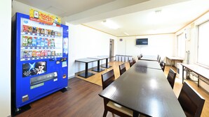 Uma sala de conferência com uma mesa comprida, cadeiras, um dispensador automático e uma televisão na parede.