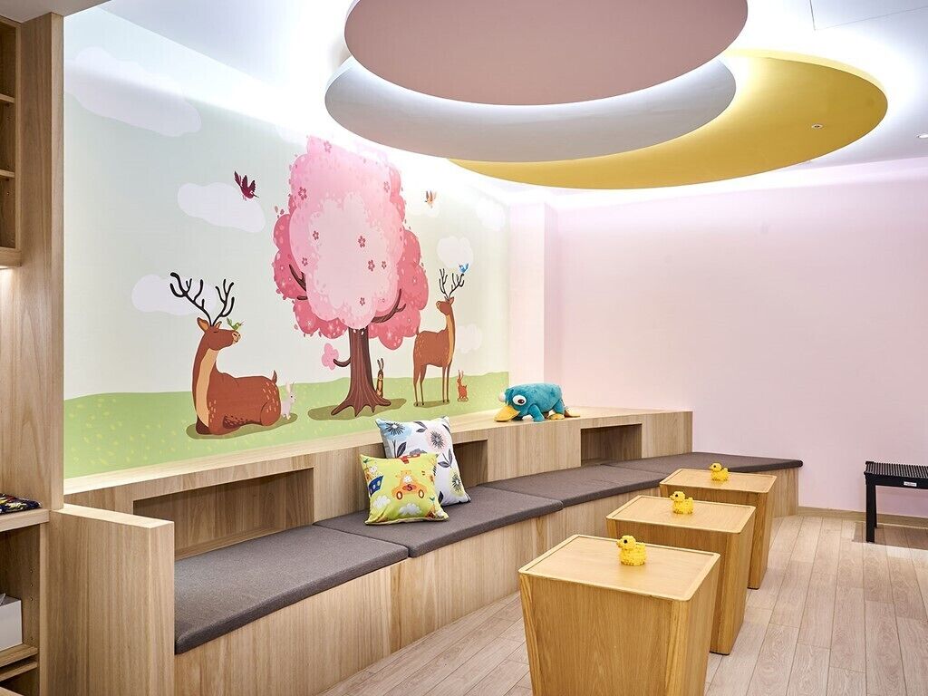Uma sala de jogos infantil com um mural de animais, assentos acolchoados e pequenas mesas.