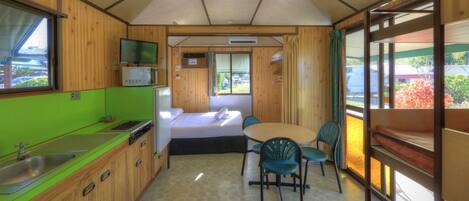 Quarto compacto com cama, pequena cozinha, área de refeições e janela com cortinas.