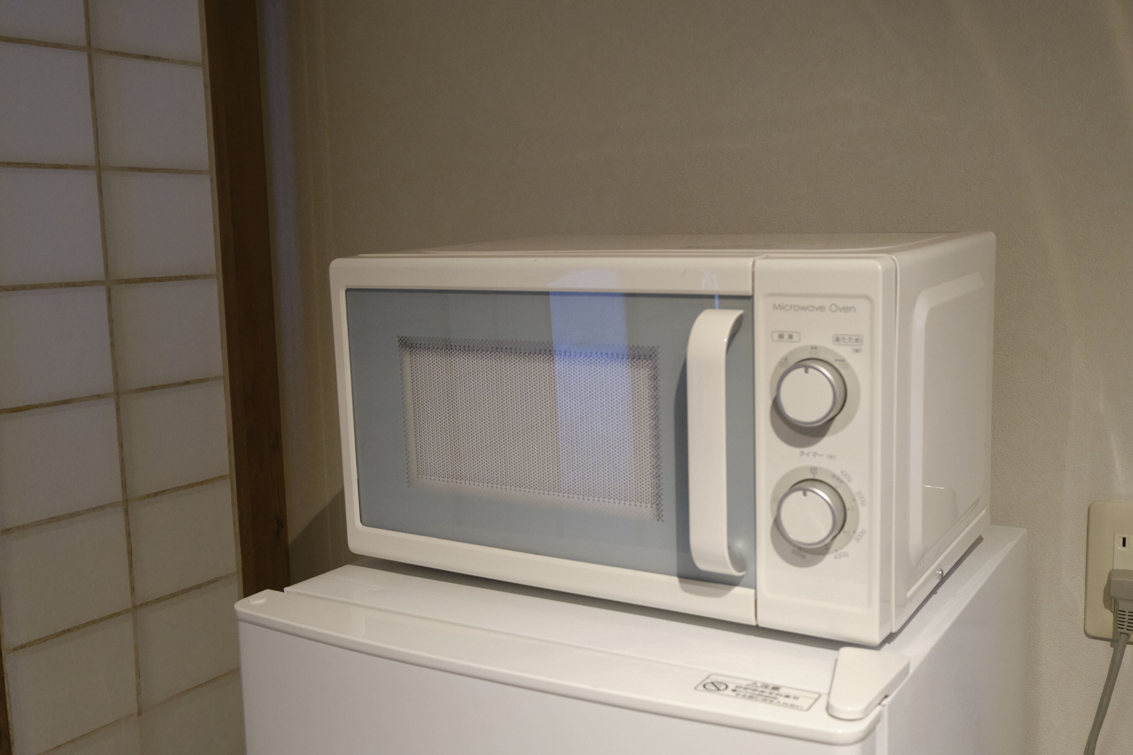 Um micro-ondas branco sobre um eletrodoméstico branco, provavelmente uma geladeira, com o cabo de alimentação conectado.