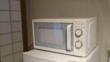 Um micro-ondas branco sobre um eletrodoméstico branco, provavelmente uma geladeira, com o cabo de alimentação conectado.