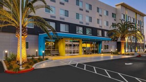 Um hotel moderno com entrada azul, palmeiras e estacionamento.