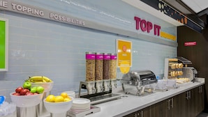 Um balcão de pequeno-almoço com diversas opções de comida, incluindo frutas, cereais e uma máquina de café.