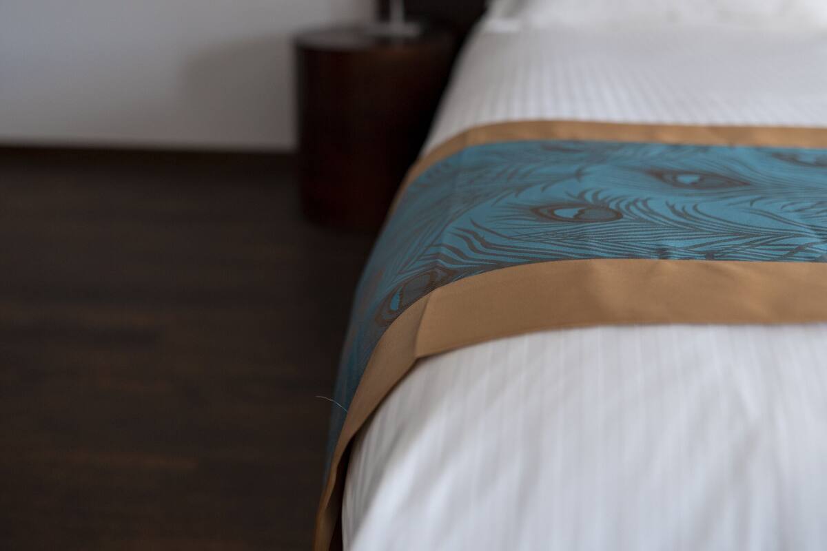 Cama bem arrumada com colcha estampada, abajur e mesa de cabeceira de madeira em quarto de hotel.