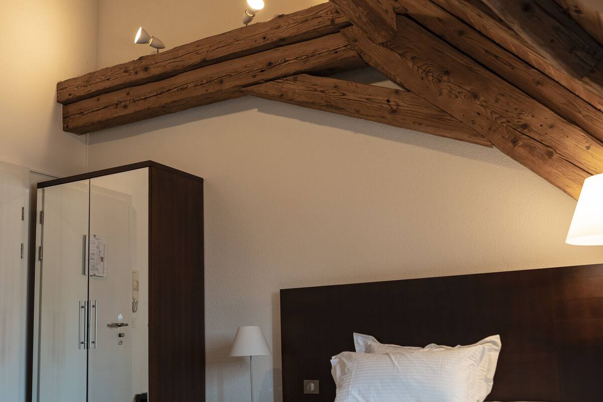 Quarto com teto de madeira, cama com roupa de cama branca, luminária de cabeceira e guarda-roupa.