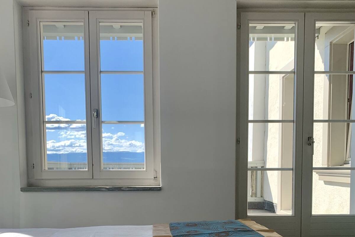Um quarto com uma cama, uma janela com vista para o céu e uma porta.