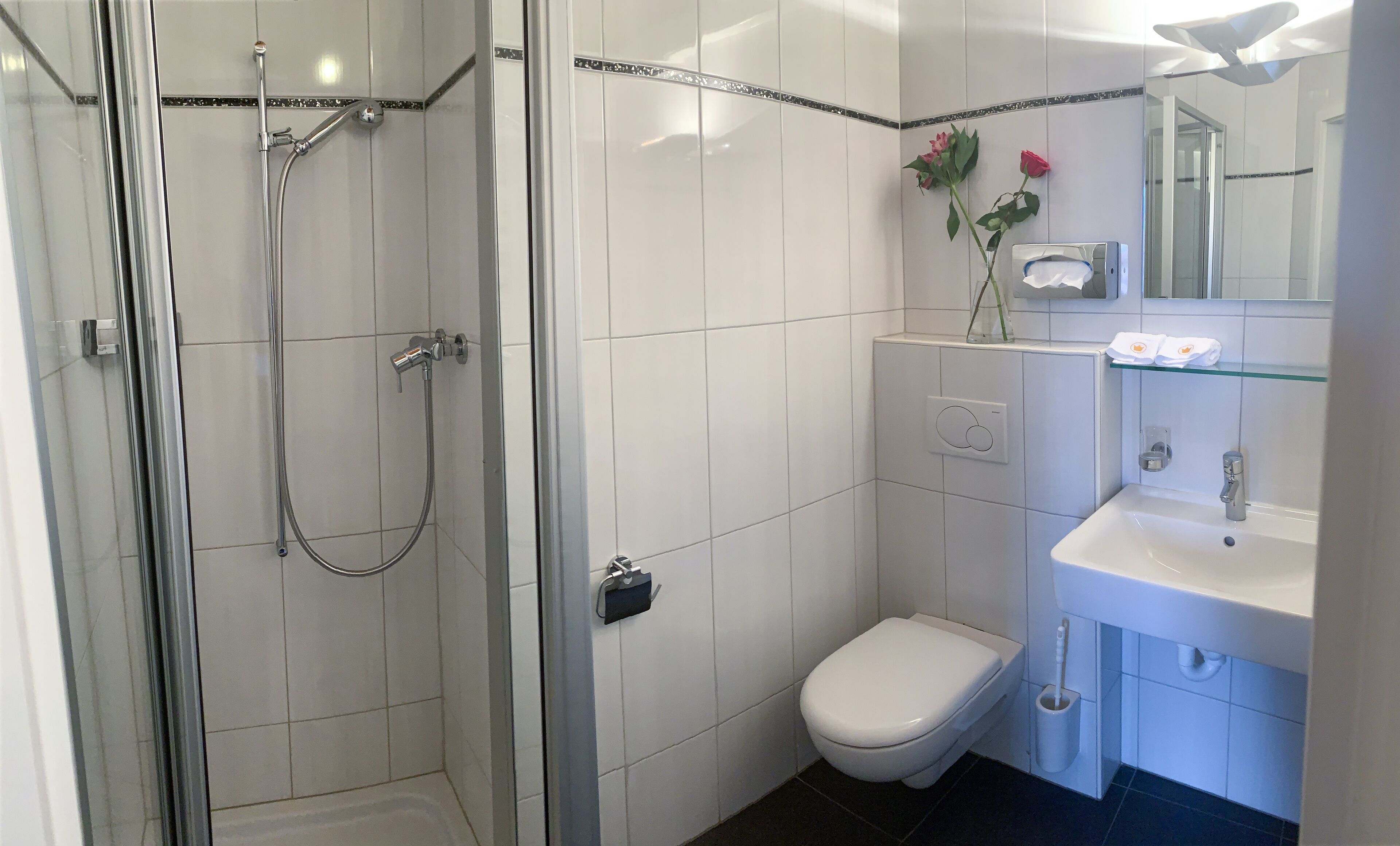 Uma casa de banho moderna com cabine de duche em vidro, sanita e lavatório com espelho em cima.