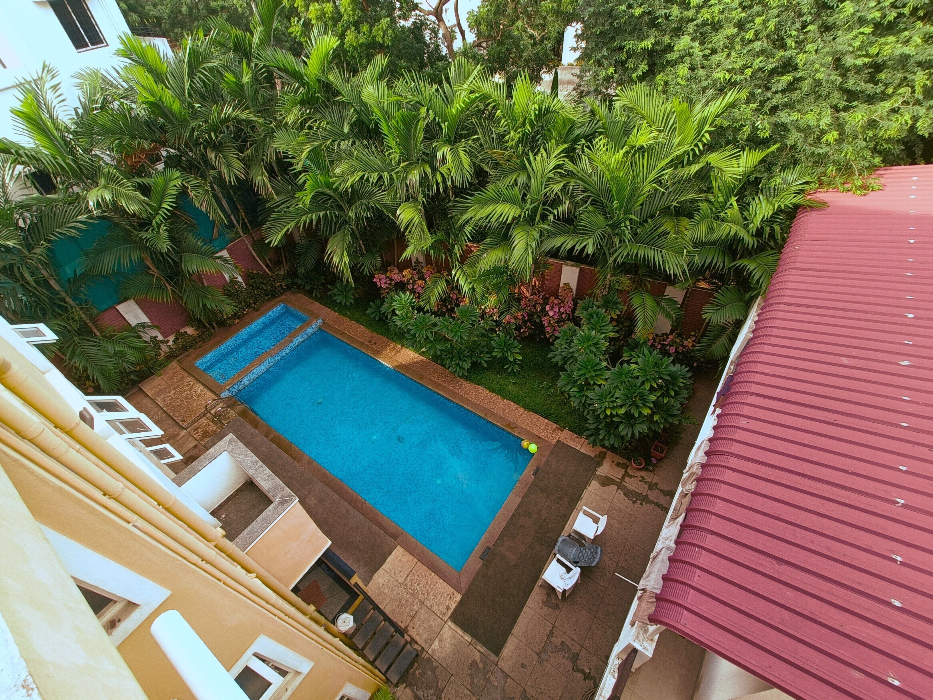 Uma piscina no terraço, cercada por vegetação exuberante e um edifício com telhado vermelho.