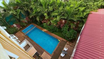 Uma piscina no terraço, cercada por vegetação exuberante e um edifício com telhado vermelho.