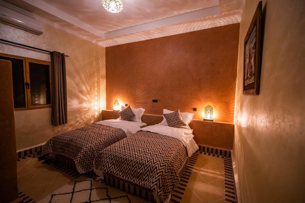 Quarto com duas camas, uma janela com cortinas e luminárias na parede.
