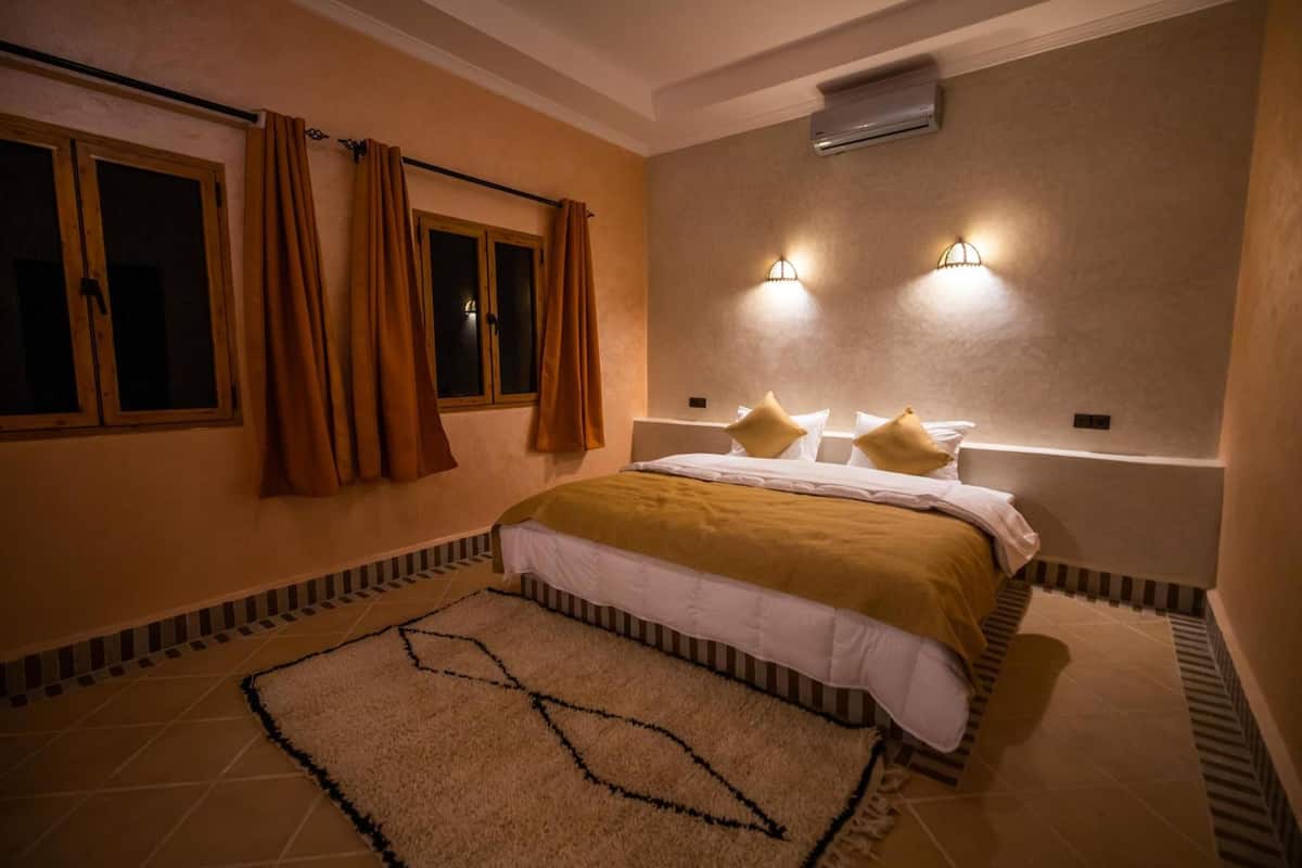 Quarto com cama, cortinas, luminárias na parede e tapete.