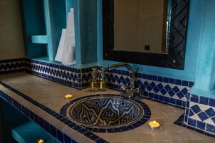 Casa de banho com lavatório em azulejo azul e branco, um espelho e um porta-toalhas.