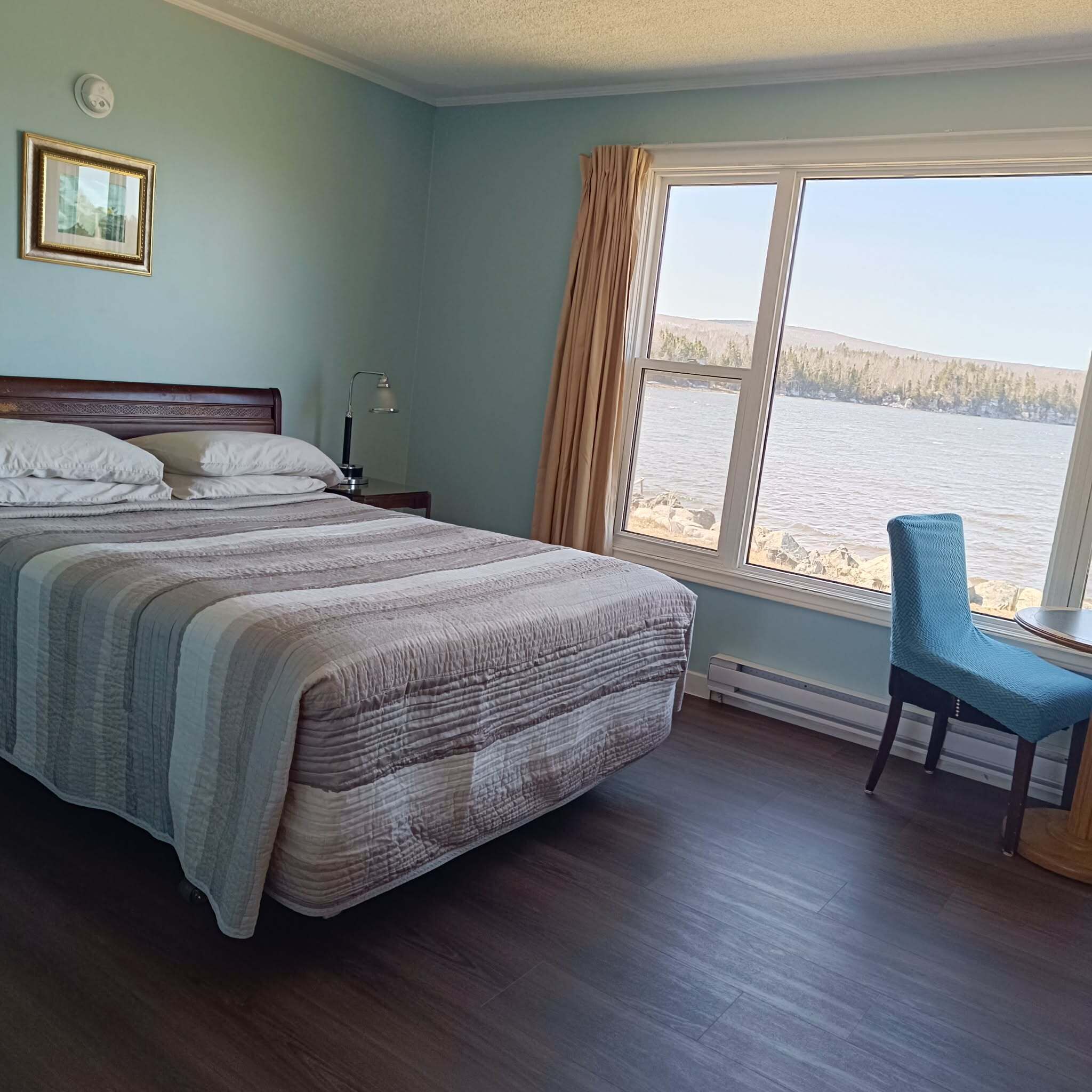 Quarto com cama, cadeira, mesa de cabeceira, luminária e janela com vista para a água.