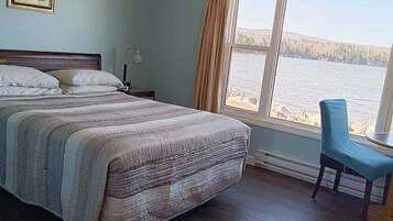 Quarto com cama, cadeira, mesa de cabeceira, luminária e janela com vista para a água.
