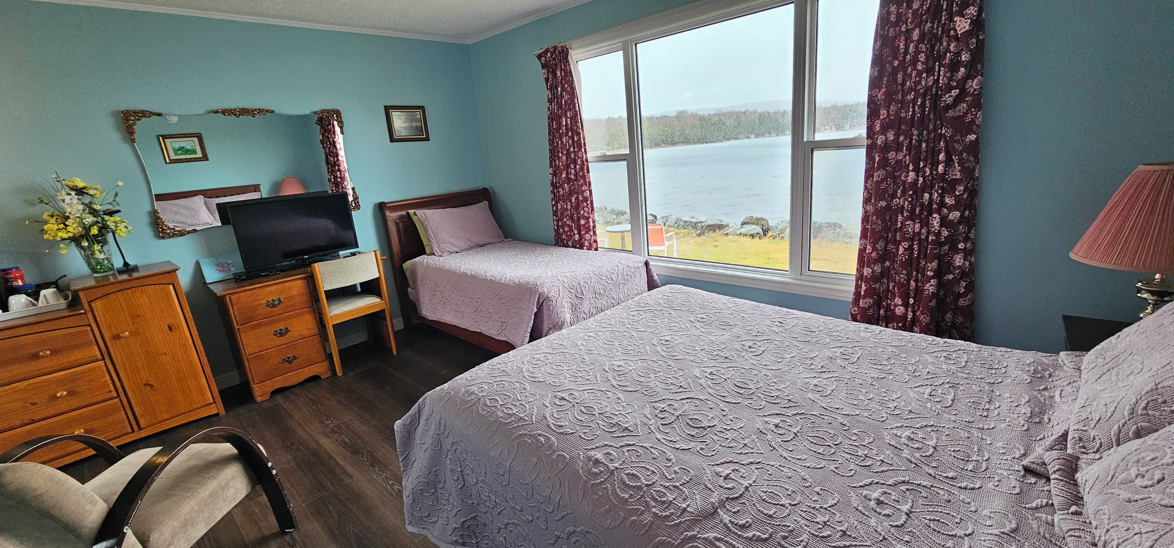 Quarto com cama, televisão, cômoda e janela com vista para um lago.